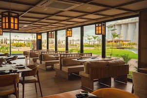 Restaurante com mesas ao ar livre, janelas amplas e lanternas penduradas.