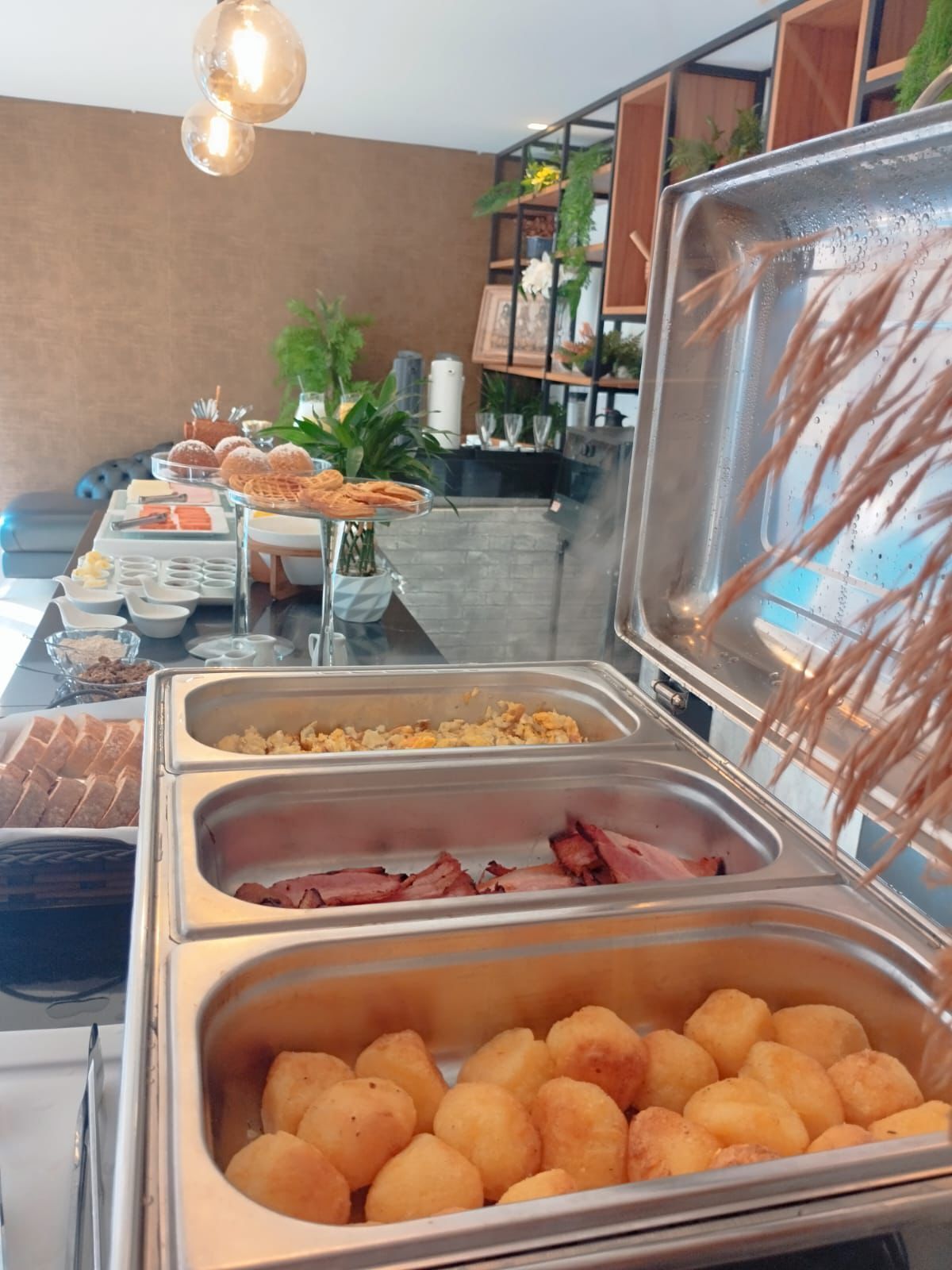 Buffet com diversos alimentos, incluindo ovos mexidos, bacon e pastéis redondos.