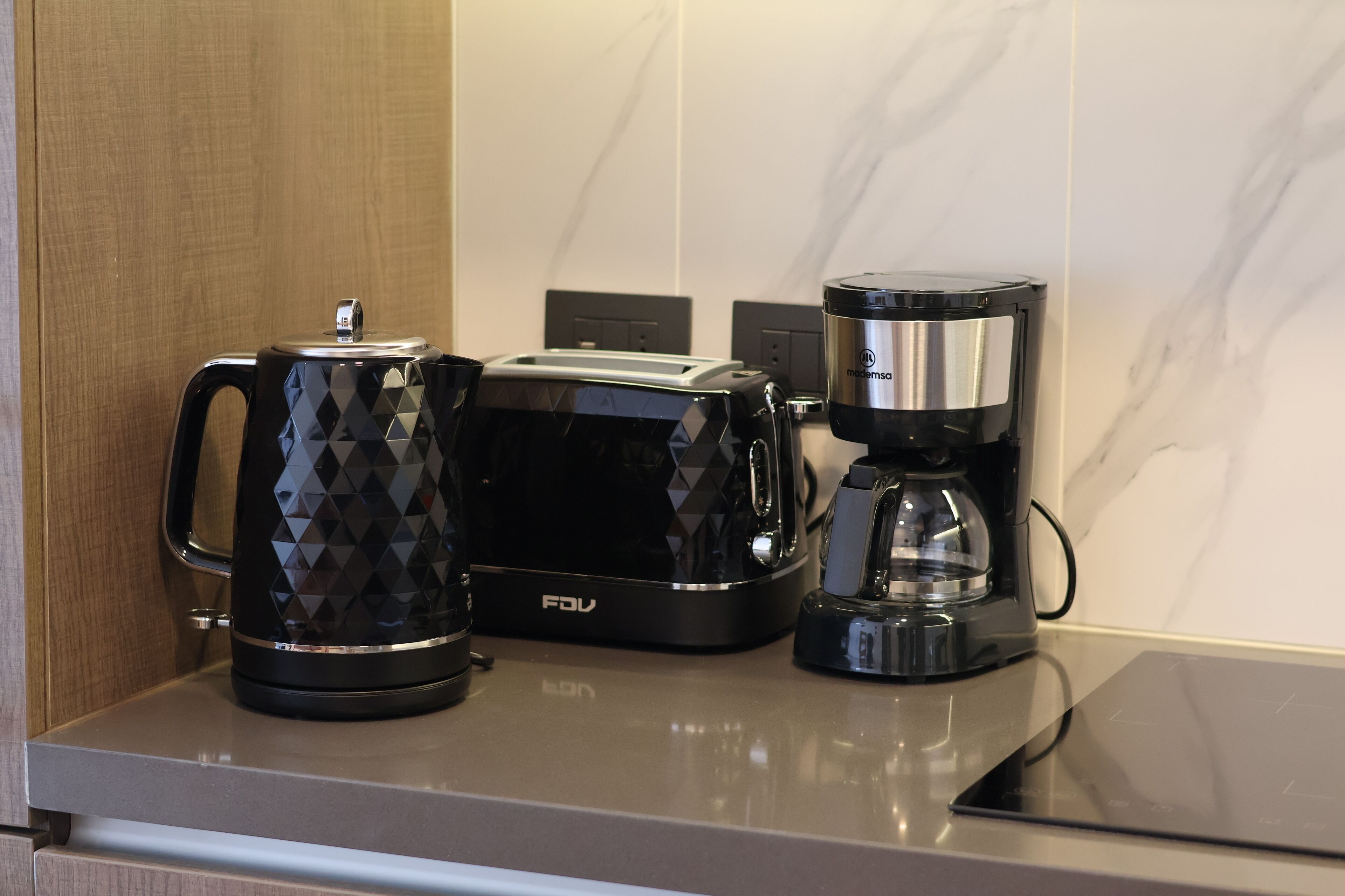 Uma bancada de cozinha com uma cafeteira, uma torradeira e uma chaleira.