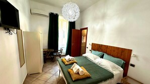 Quarto com cama, escrivaninha, cadeira, televisão e luminária de teto.