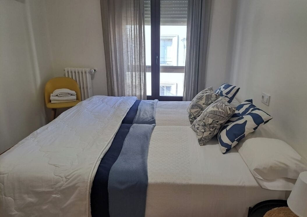 Quarto de hotel com cama, uma cadeira e janela com cortinas.