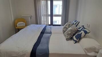 Quarto de hotel com cama, uma cadeira e janela com cortinas.