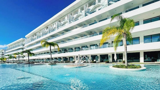 Um hotel moderno com uma piscina grande, várias varandas e palmeiras.