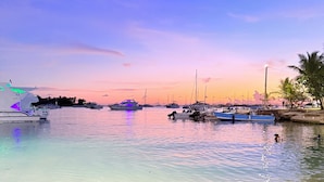 Uma praia com águas cristalinas, barcos e um céu ao pôr do sol.