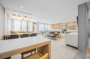 Um lobby de hotel moderno com área de refeições, assentos e balcão de recepção.