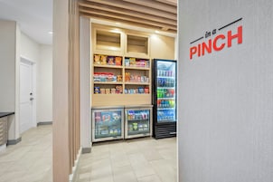 Uma área de máquinas de venda automática de lanches e bebidas, com várias prateleiras repletas de produtos diversos e um refrigerador.