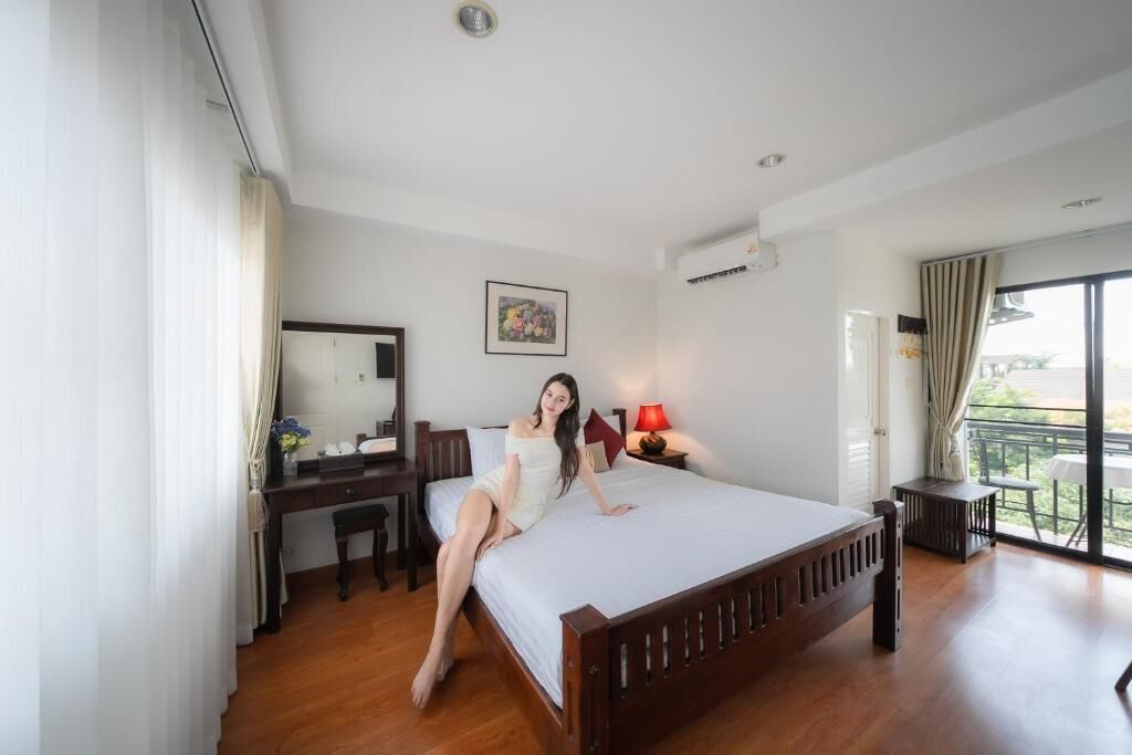 Quarto de hotel com cama, escrivaninha, cadeira, mesa de cabeceira com abajur, janela ampla e varanda.
