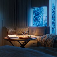 Um quarto acolhedor com sofá, uma mesinha com um livro e copos, e uma janela com vista para árvores.