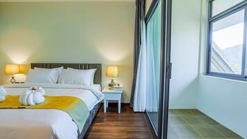 Quarto de hotel com cama, duas luminárias de cabeceira, uma mesinha de cabeceira pequena, janela com cortinas e vista para o exterior.