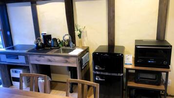 Uma área de cozinha com mesa de madeira, cadeiras, pia e máquina de café. Há também eletrodomésticos pretos em uma prateleira.