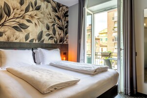 Quarto de hotel com cama, almofadas e vista para prédios pela janela.