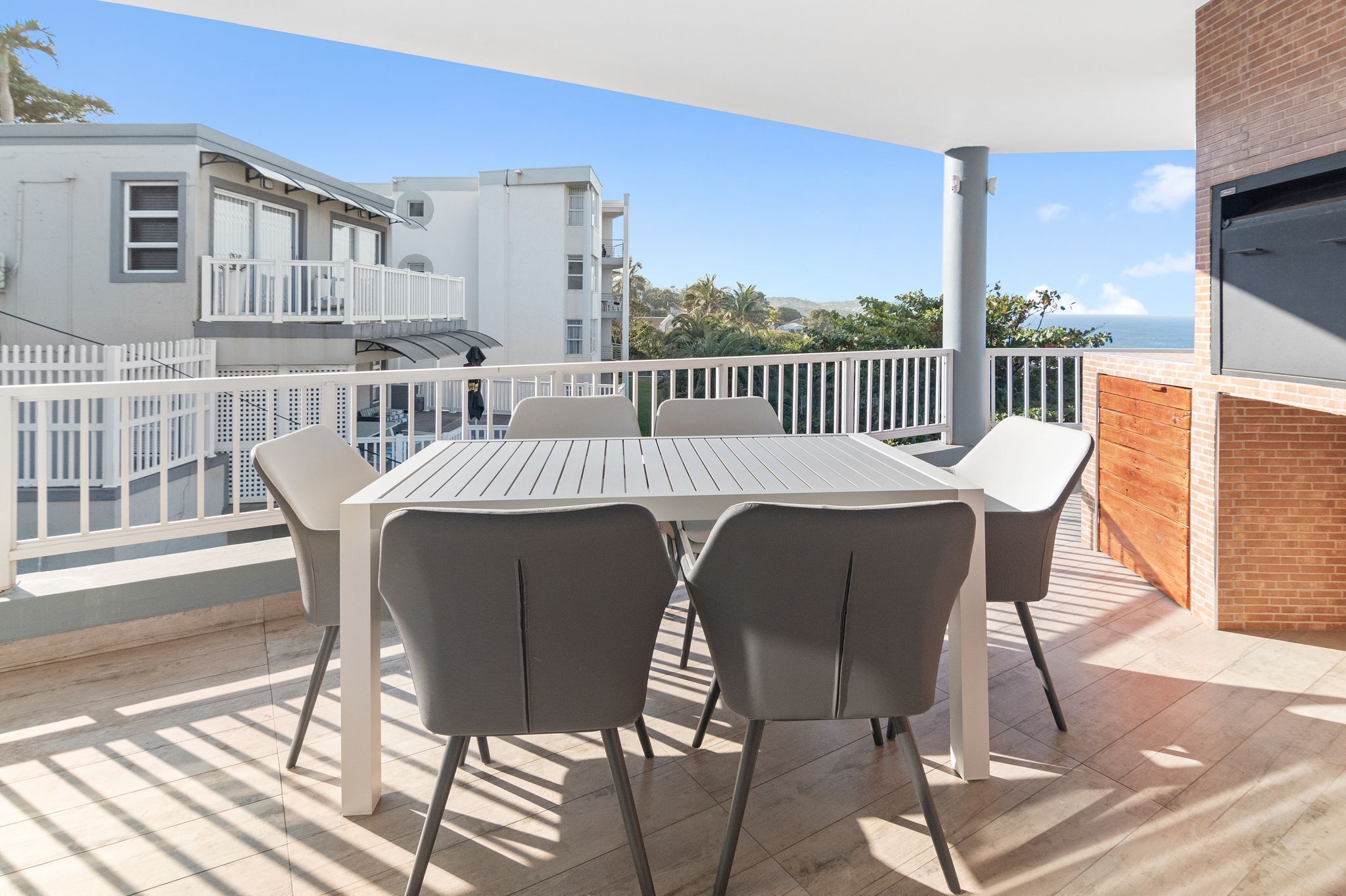 Varanda com mesa e cadeiras, uma televisão e vista para o oceano e edifícios.