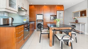 Uma cozinha moderna com armários de madeira, eletrodomésticos de aço inoxidável e um espaço de jantar com mesa e cadeiras.