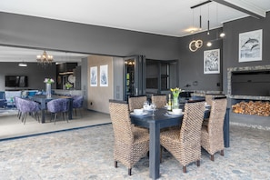 Uma área de jantar moderna, com mesa escura e cadeiras estampadas, cozinha ao fundo e obras de arte nas paredes.