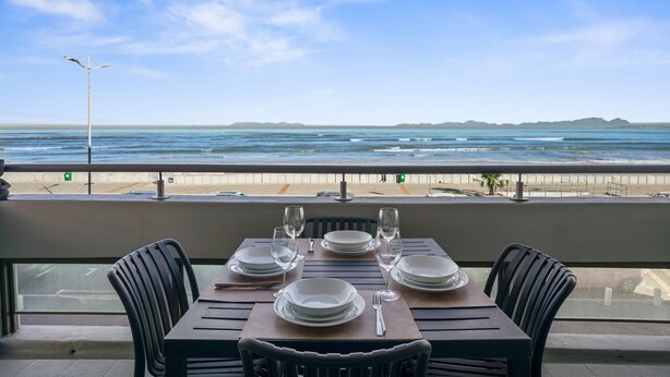 Mesa posta para refeição com vista para o mar e a praia.