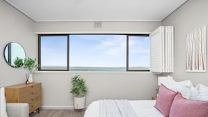 Quarto com uma janela grande, uma cama, uma cômoda, um espelho e uma planta.