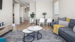 Uma sala de estar moderna com um sofá cinzento, uma mesa de centro e uma área de jantar com uma mesa e cadeiras brancas.