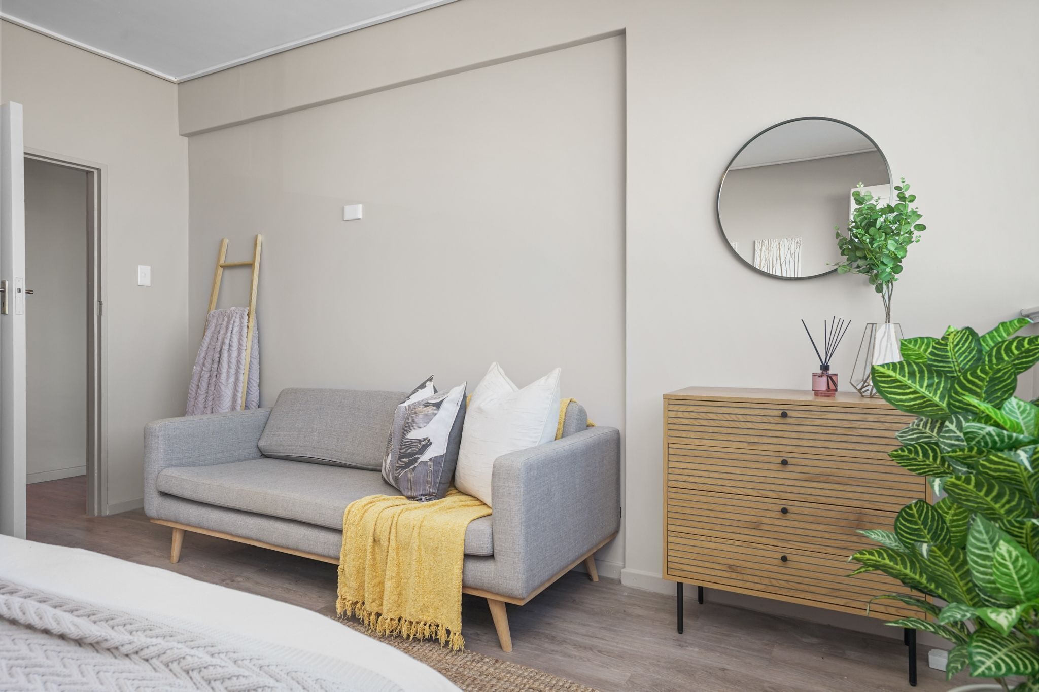 Um quarto moderno com um sofá cinzento, cómoda de madeira e um espelho na parede.