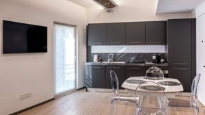 Cozinha moderna com armários escuros, bancada de mármore e área de jantar com mesa e cadeiras de vidro.