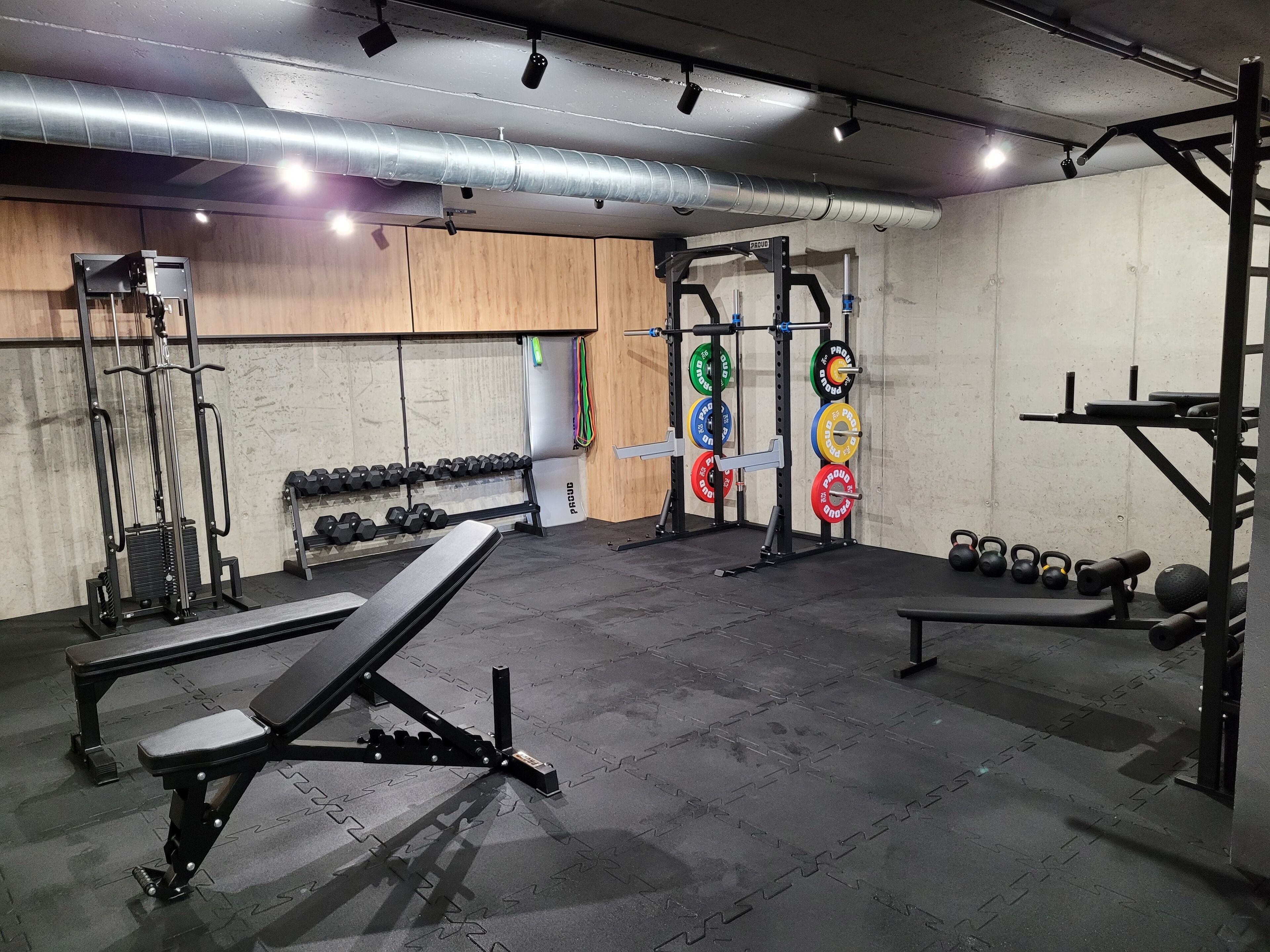 Uma academia com equipamentos de musculação, bancos e suporte para agachamento.