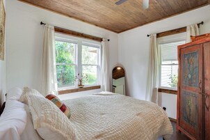 Quarto com uma cama grande, duas janelas com cortinas, teto de madeira e um armário de madeira com obras de arte.