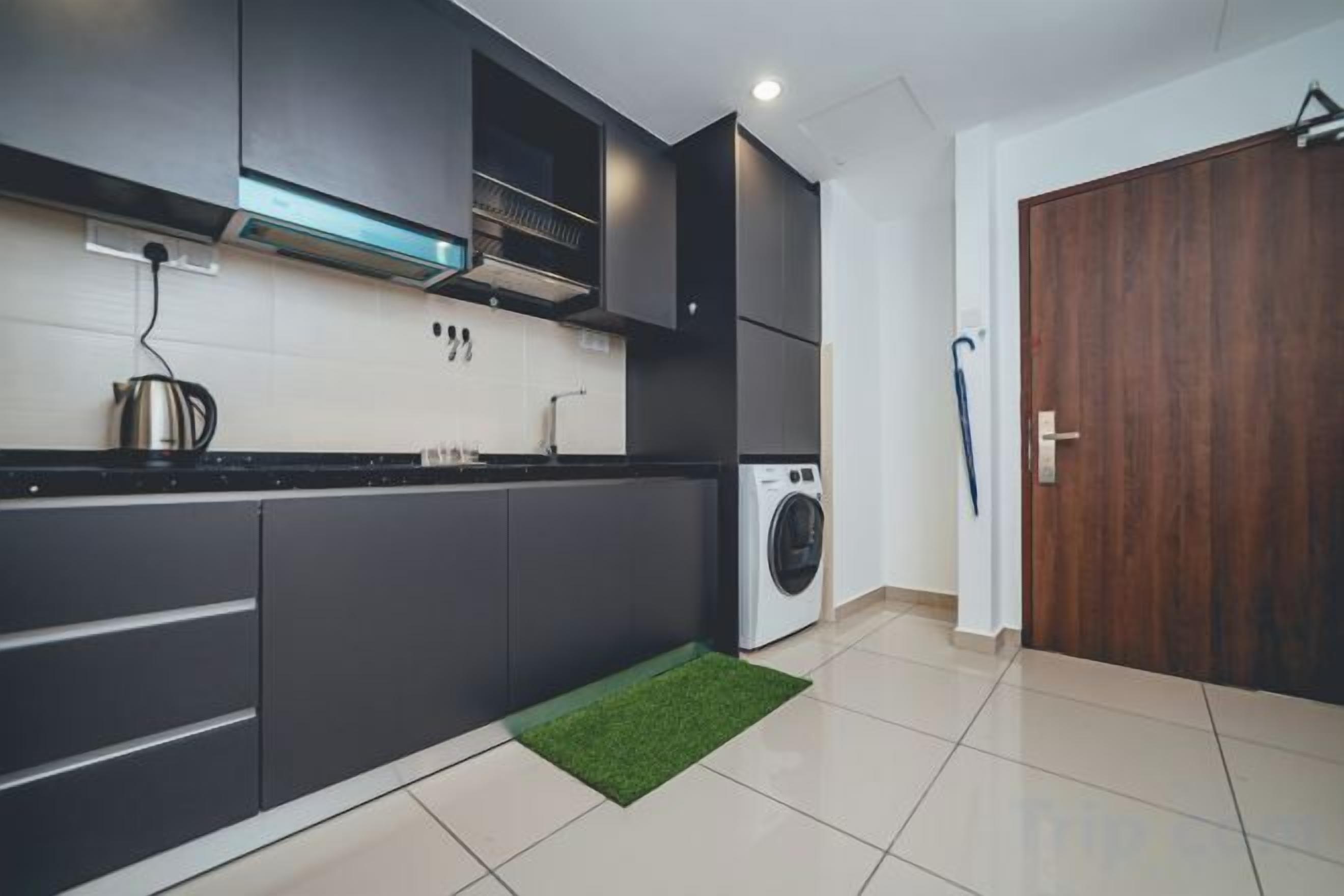 Uma cozinha moderna com armários escuros, uma máquina de lavar e um tapete verde.