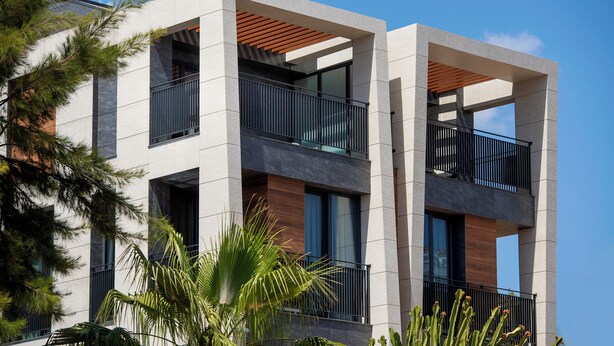 Um edifício moderno de vários andares com varandas, janelas amplas e uma combinação de painéis de concreto e madeira.