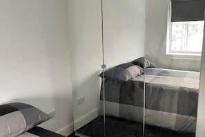 Quarto com cama, divisória de vidro e janela.