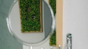 Casa de banho com espelho, porta-toalhas e uma pequena planta verde.