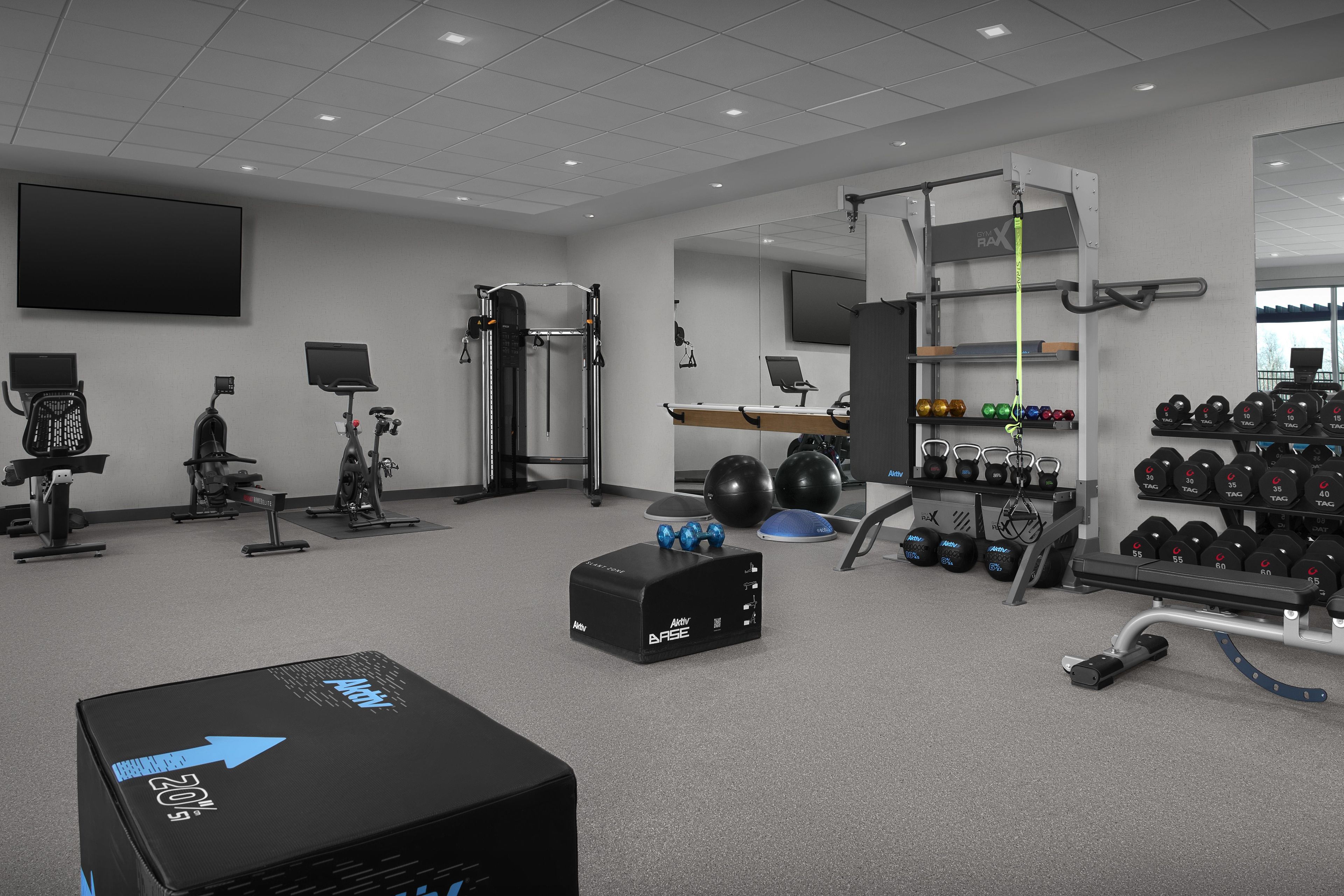 Academia com diversos equipamentos de exercícios, incluindo esteira, bicicleta ergométrica, banco de peso e pesos livres.