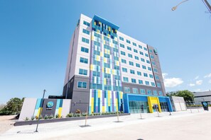 Um hotel moderno com fachada destacada em azul e amarelo, várias janelas e céu claro.