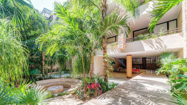 Interior de hotel moderno com um pátio central, área de estar ao ar livre e vegetação exuberante.