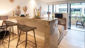 Uma cozinha moderna com bancada de granito, banquetas e área de jantar com televisão.