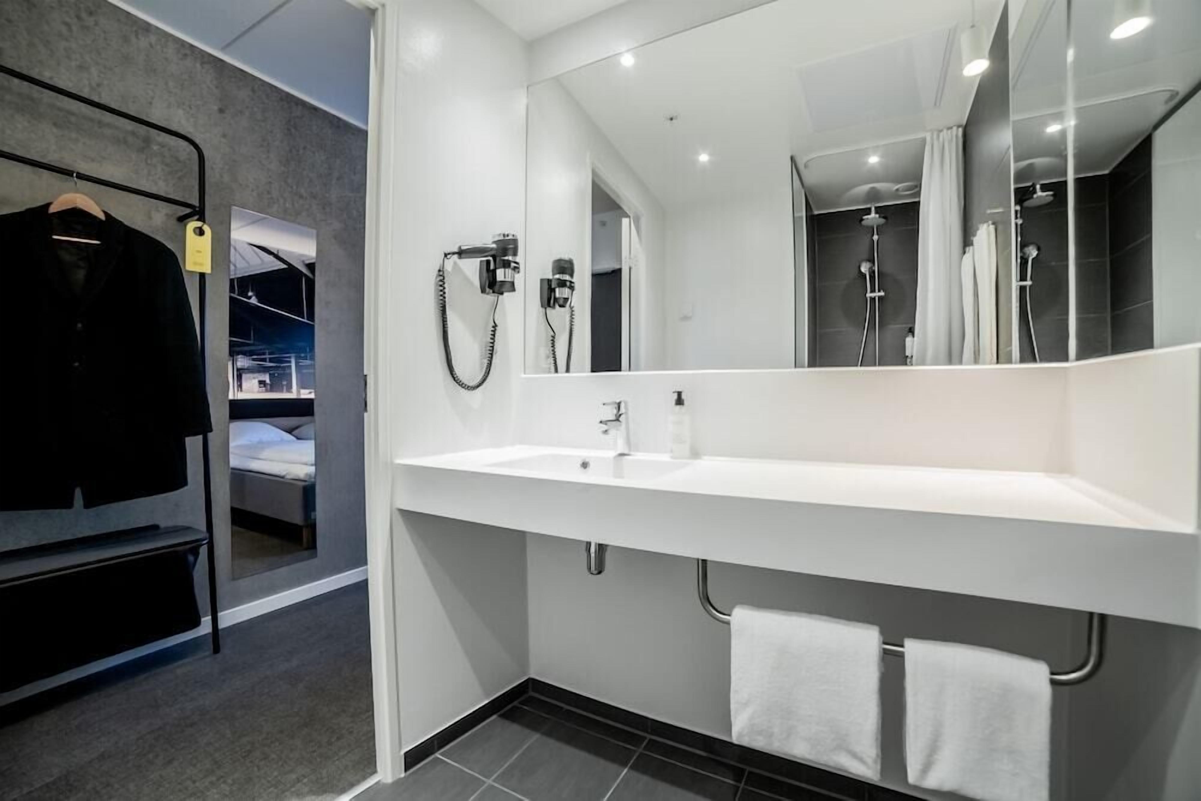 Uma casa de banho moderna com um espelho grande, uma sanita branca e uma área de duche.