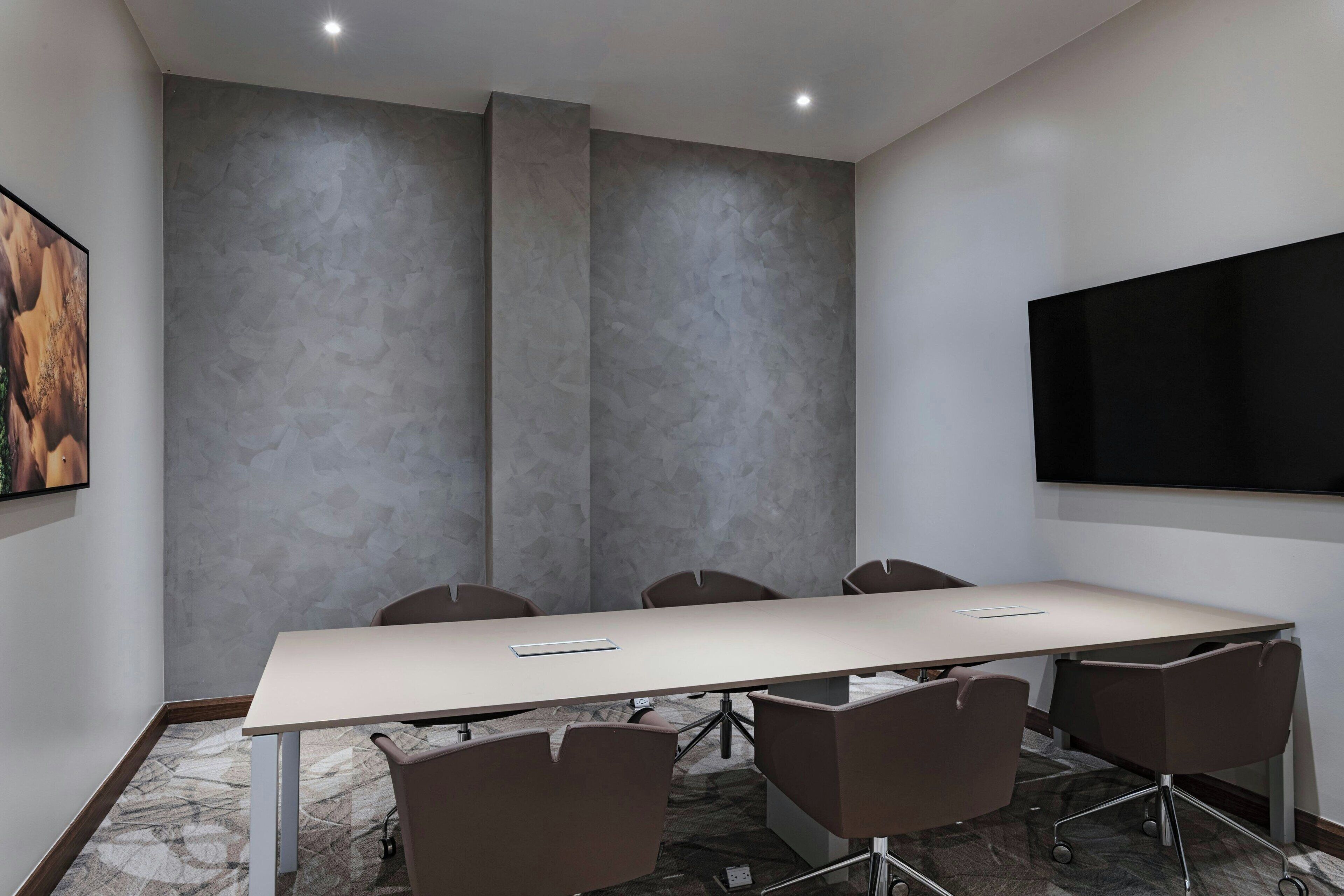 Uma sala de conferências com uma mesa comprida, seis cadeiras, um grande ecrã e uma parede texturizada.