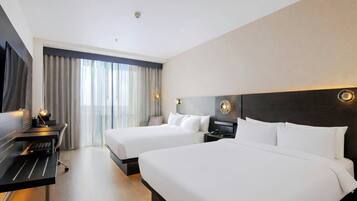 Quarto de hotel com duas camas, uma mesa, uma televisão e uma janela grande com cortinas.