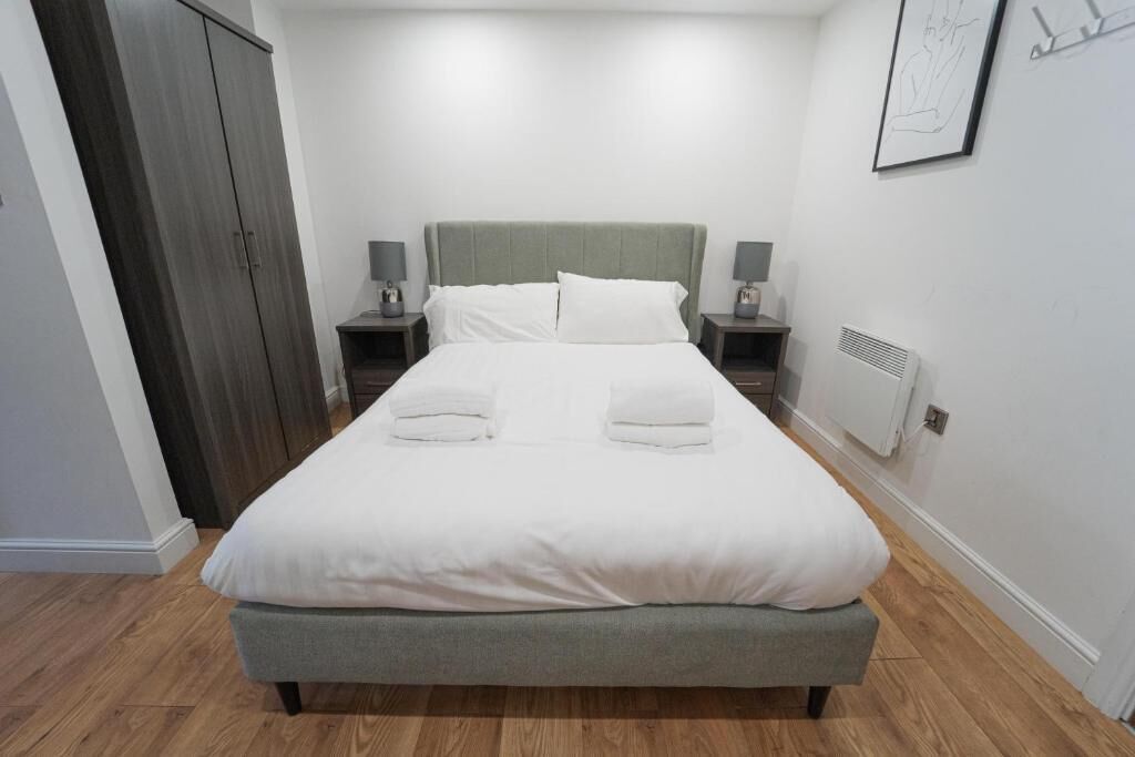 Quarto bem arrumado com cama, mesas de cabeceira, guarda-roupa e radiador.