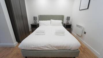 Quarto bem arrumado com cama, mesas de cabeceira, guarda-roupa e radiador.