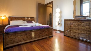Quarto com cama de madeira, cômoda e penteadeira com iluminação.