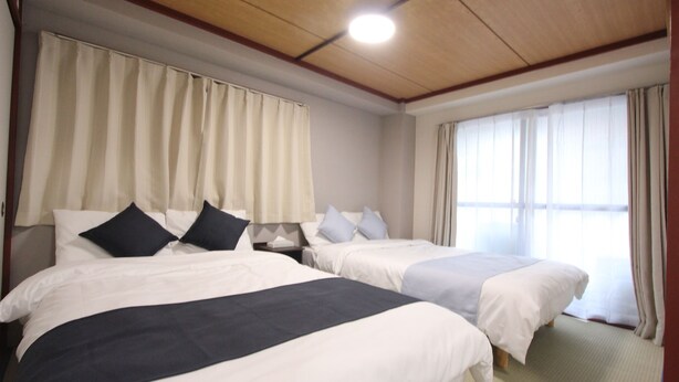 Quarto de hotel com duas camas, teto de madeira e janelas amplas com cortinas.
