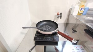 Uma cozinha com fogão, frigideira, espátula e um frasco de sabonete líquido.