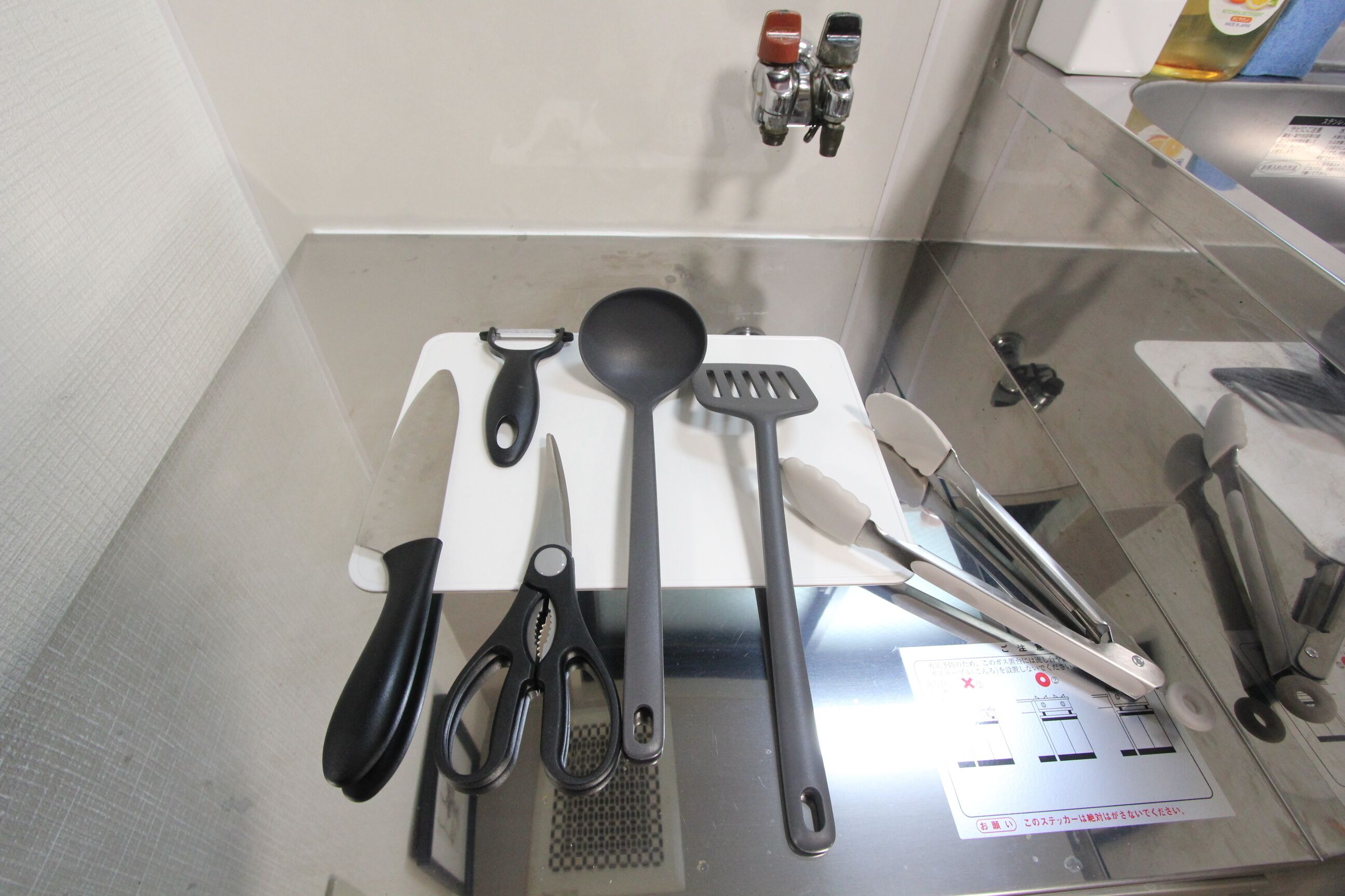 Uma bancada de cozinha com diversos utensílios, incluindo tesoura, ralador, espátula e concha.