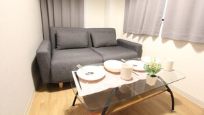 Uma sala de estar moderna com um sofá cinzento, uma mesa de centro de vidro com um descanso para prato e uma pequena planta em vaso.