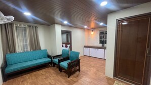 Sala de estar com sofá, cadeiras, uma mesinha, um armário de madeira e um espaço de cozinha com bancada e armários.