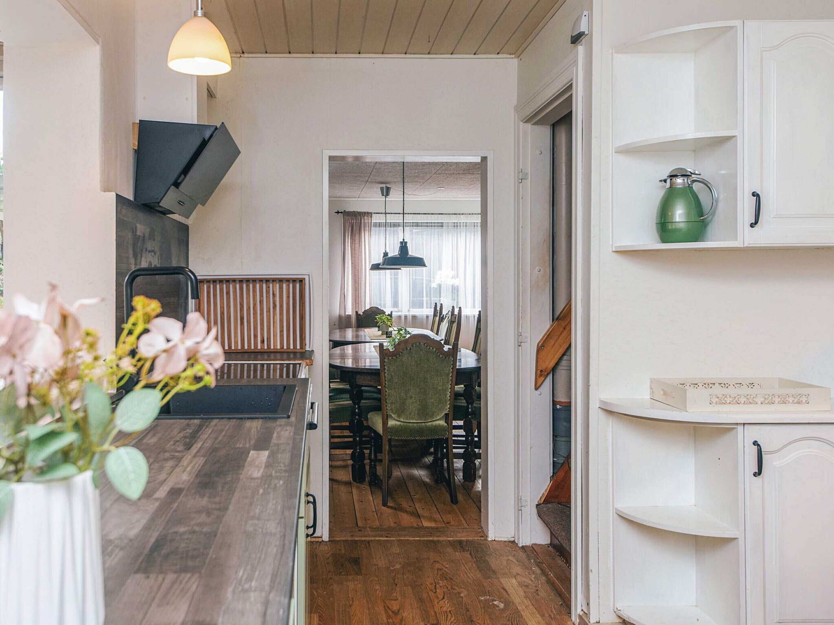 Cozinha moderna com piso de madeira, área de jantar com mesa e cadeiras, e um armário branco com uma chaleira verde.