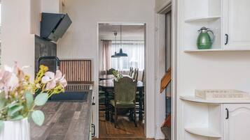 Cozinha moderna com piso de madeira, área de jantar com mesa e cadeiras, e um armário branco com uma chaleira verde.