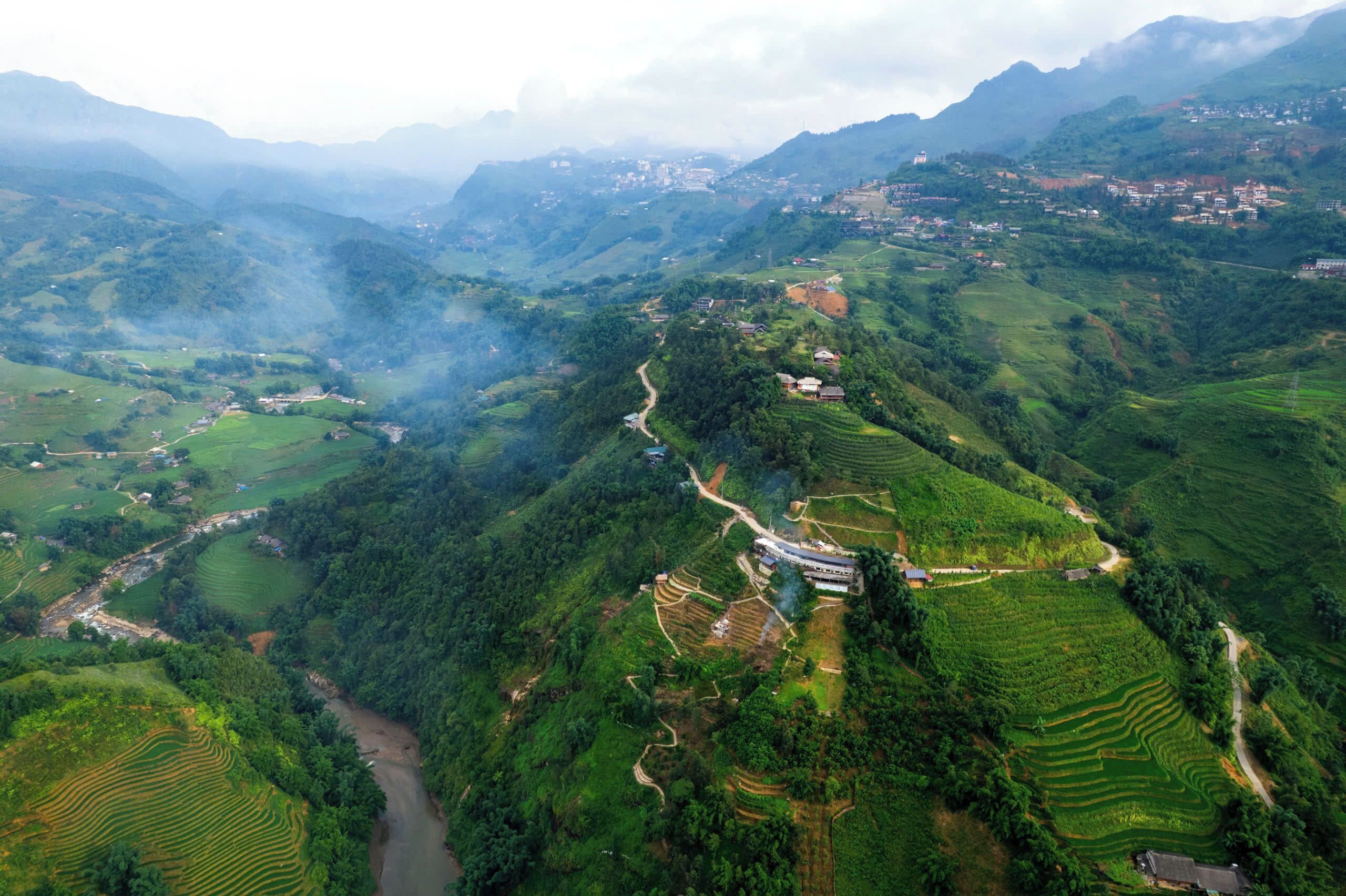Paisagem montanhosa com campos em terraços e alguns edifícios dispersos.