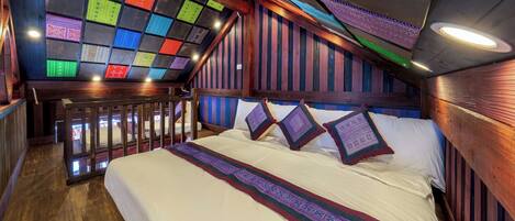 Quarto com uma cama grande, cabeceira de madeira e vista para o exterior através de uma janela com padrões coloridos.