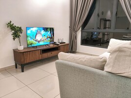 Uma sala de estar com televisão de tela plana sobre um suporte de madeira, uma planta em vaso e um sofá.