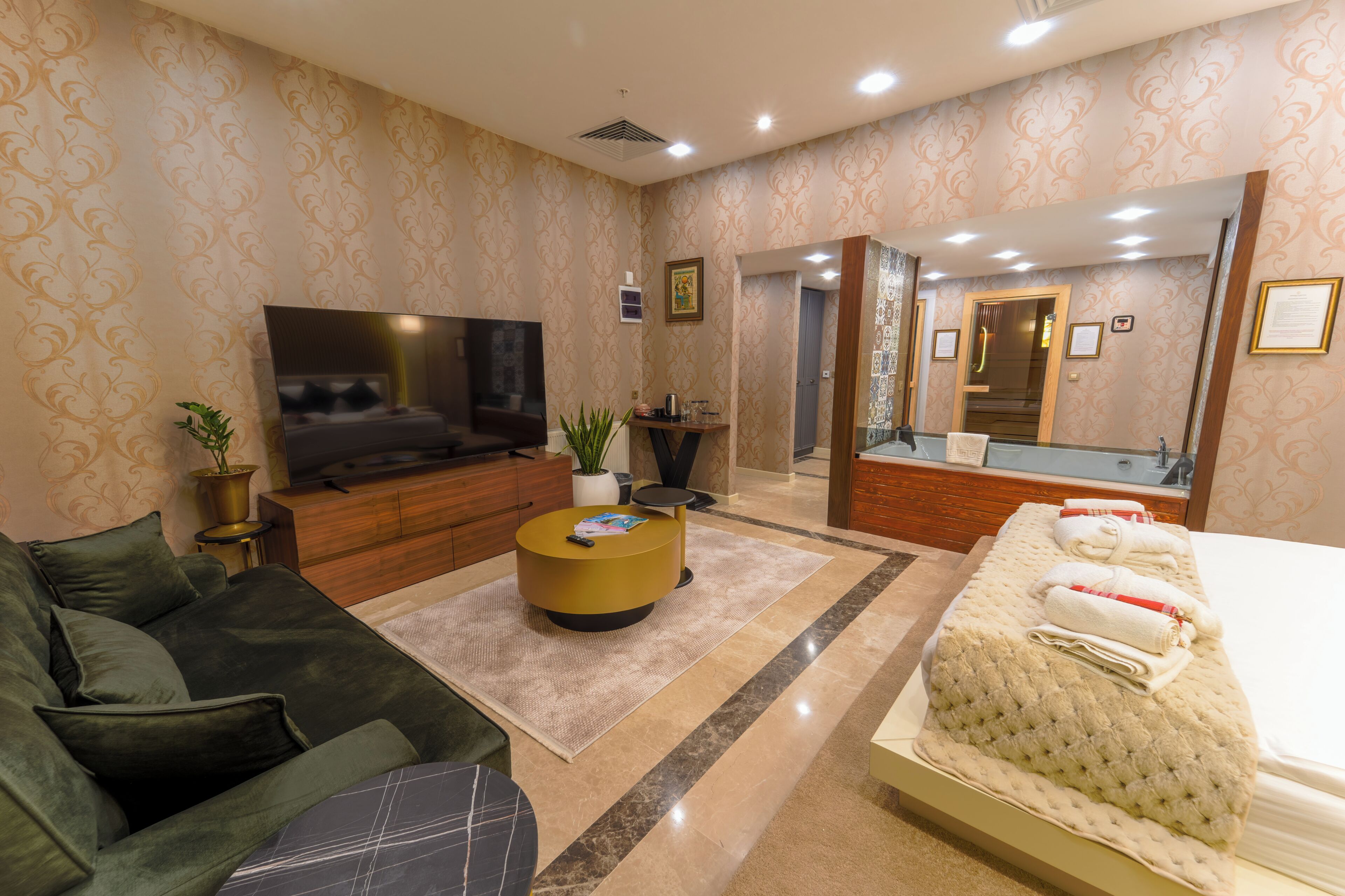 Quarto de hotel com televisão, sofá, puf, cama e espelho de banheiro.